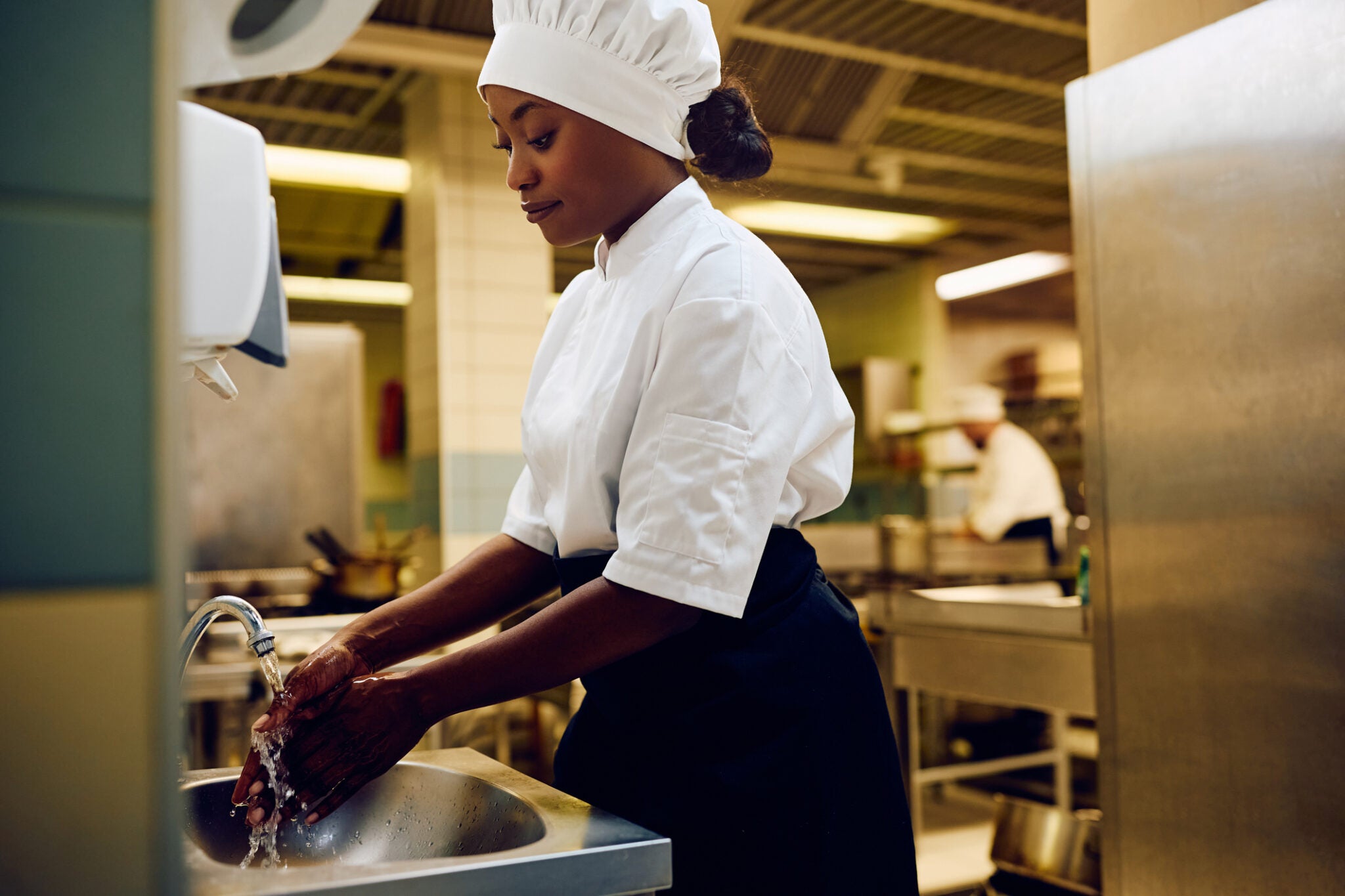 Black female chef washing hands under kitchen sink in a restaurant ...